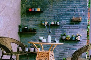 Quarto com parede de tijolos, móveis de vime e prateleiras com plantas e objetos decorativos.