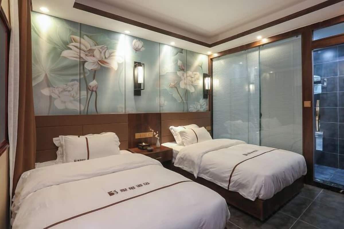 Quarto de hotel com duas camas, um grande painel floral, uma porta de correr de vidro e uma cabeceira de madeira.