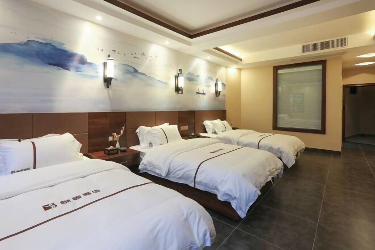 Quarto de hotel com três camas, um mural grande na parede e uma porta deslizante para um banheiro.