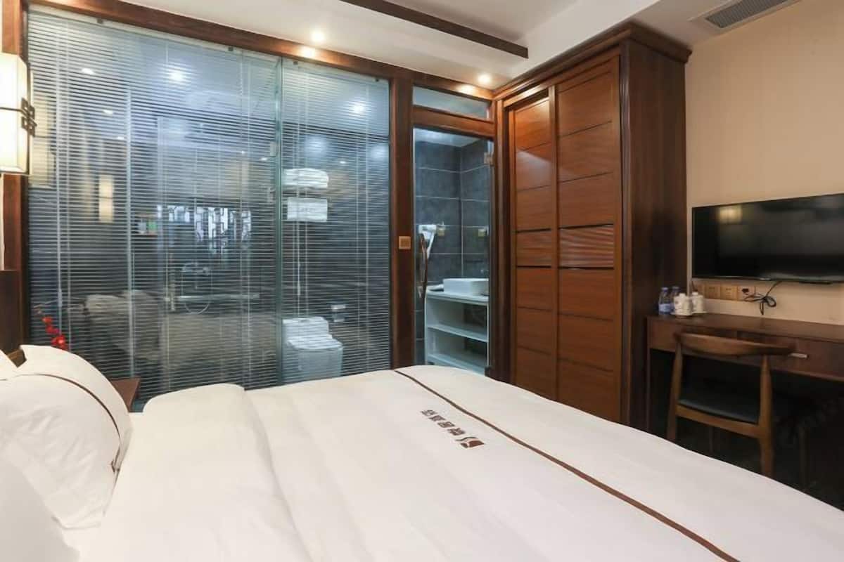 Quarto de hotel com cama, televisão, guarda-roupa de madeira e porta de vidro para uma casa de banho.