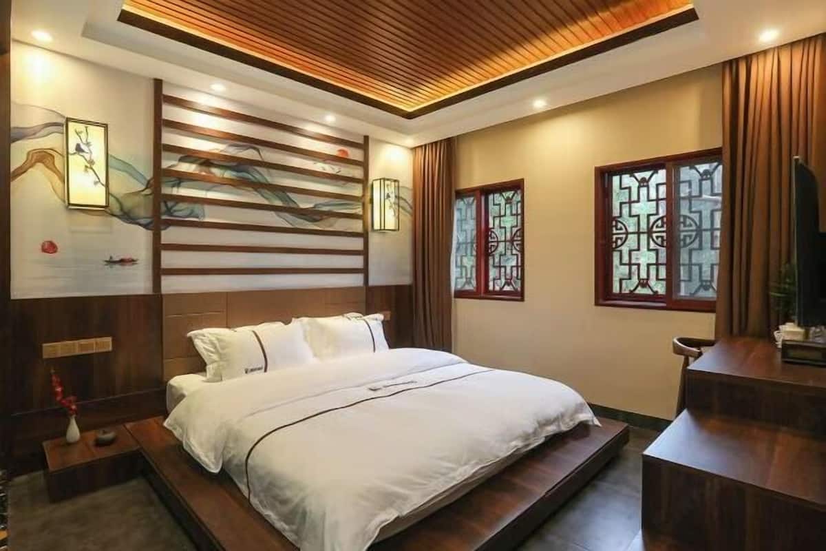 Quarto com cama, painéis de madeira, mesa de cabeceira e televisão.