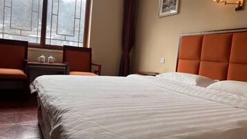 Quarto de hotel com uma cama grande, uma mesa com cadeira, uma janela com cortinas e uma luminária fixada na parede.