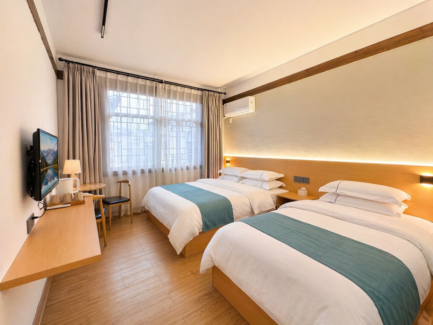 Quarto de hotel com duas camas, uma escrivaninha com cadeira, uma televisão e uma janela com cortinas.