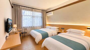 Quarto de hotel com duas camas, uma escrivaninha com cadeira, uma televisão e uma janela com cortinas.