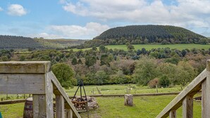 Um deck de madeira com vista para uma paisagem rural, com uma colina e árvores.
