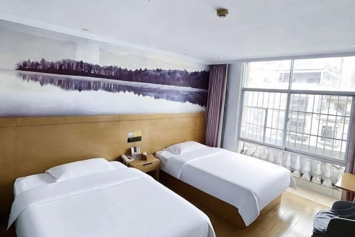 Quarto de hotel com duas camas, uma janela grande e um mural na parede.