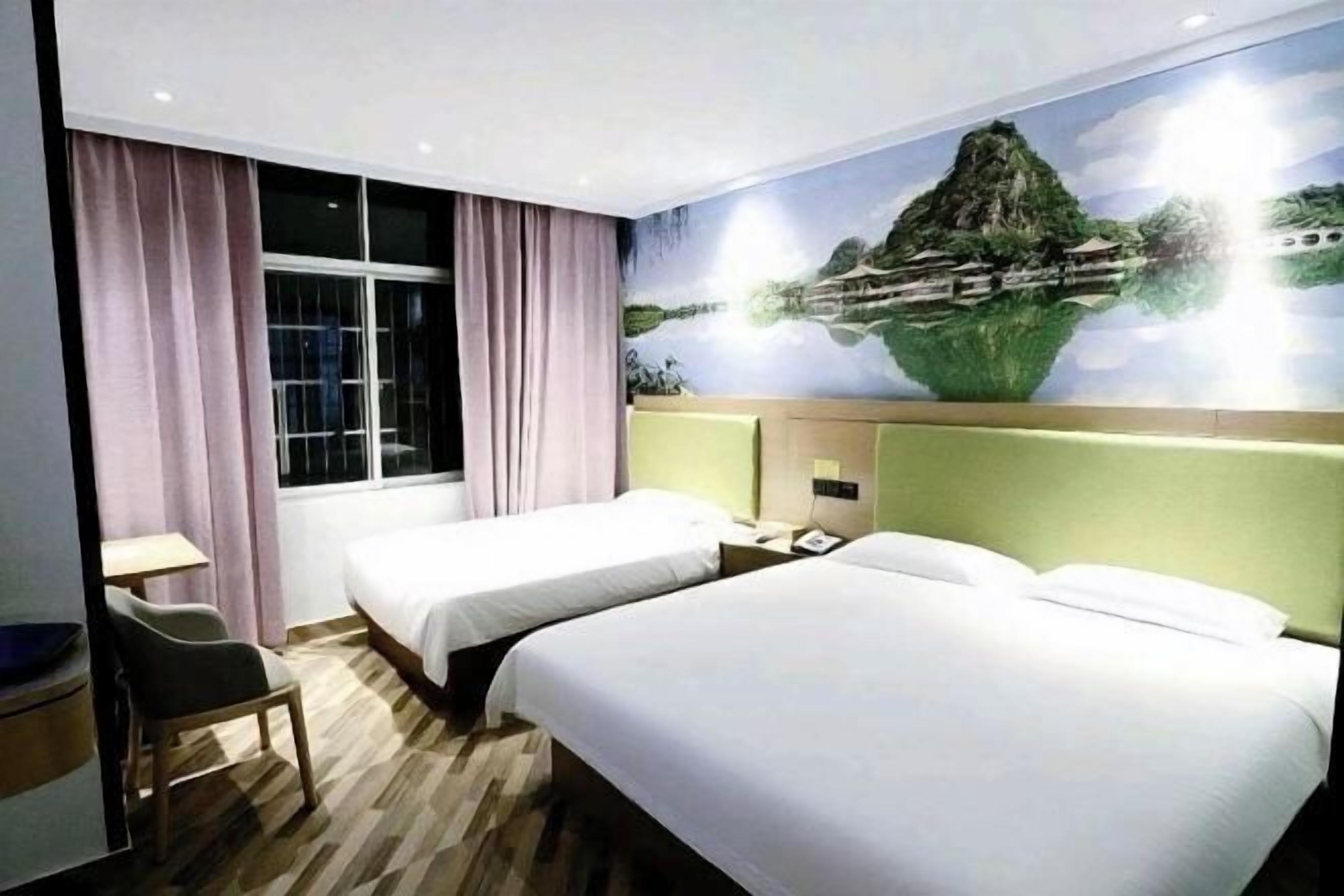 Quarto de hotel com duas camas, uma escrivaninha, uma cadeira, uma janela com cortinas e um mural com paisagem de montanhas.