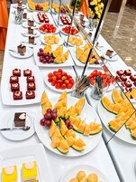 Uma mesa de buffet com diversos alimentos, incluindo sobremesas, frutas e legumes.