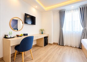 Quarto de hotel com escrivaninha, cadeira, televisão e cama.