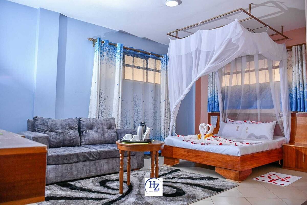Quarto de hotel com cama, sofá, uma mesinha e janela com cortinas.