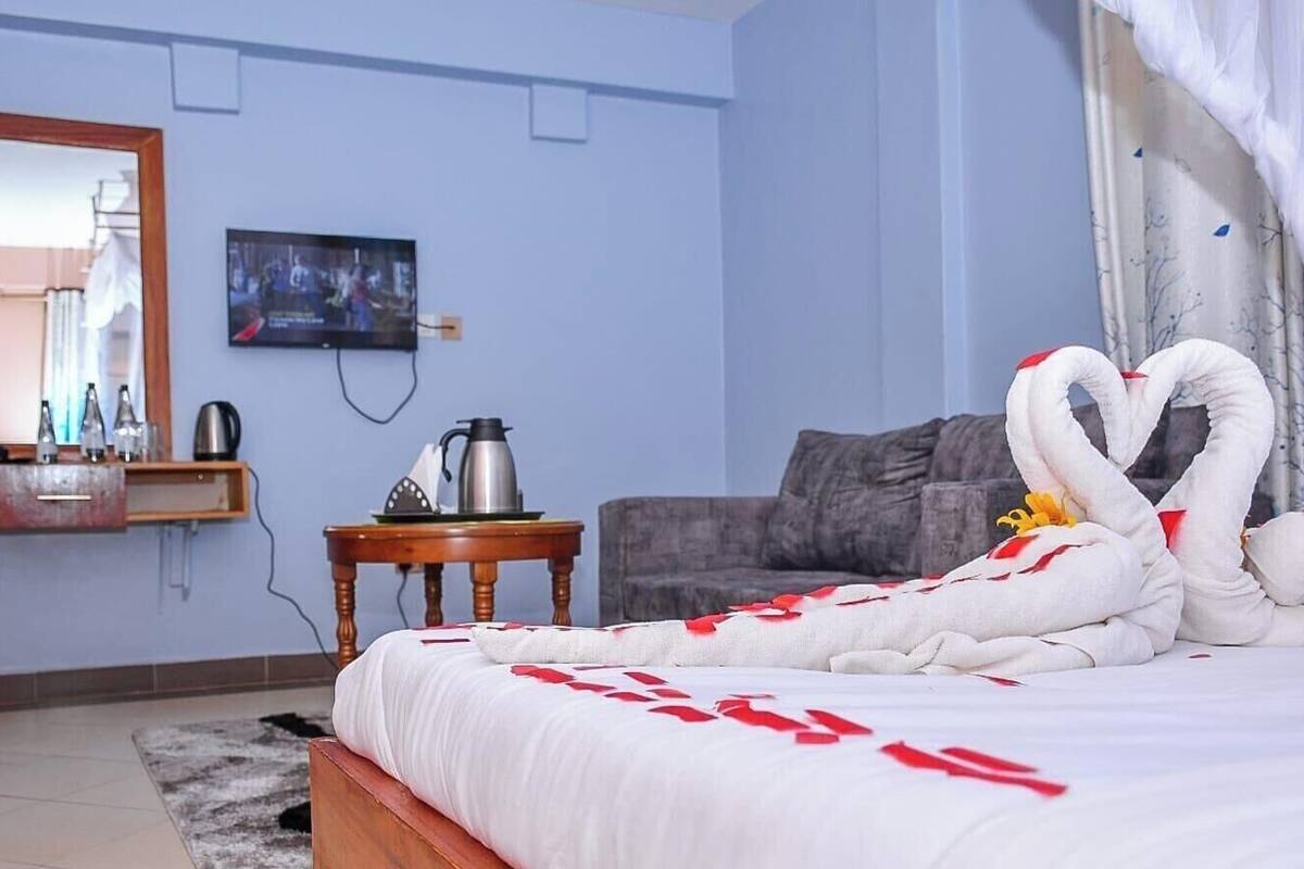 Quarto de hotel com cama, televisão, mesa de centro, sofá e espelho.