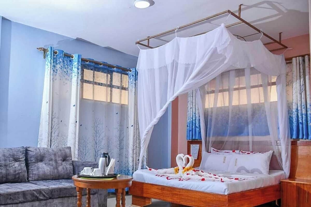 Quarto com uma cama, um sofá, uma mesinha com chaleira e cortinas.