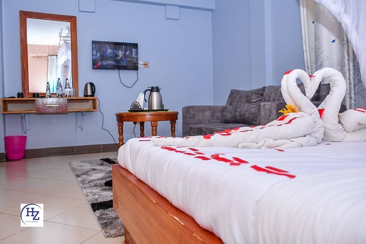 Quarto de hotel com cama, mesa de cabeceira de madeira, mesinha de centro, sofá, televisão e espelho.