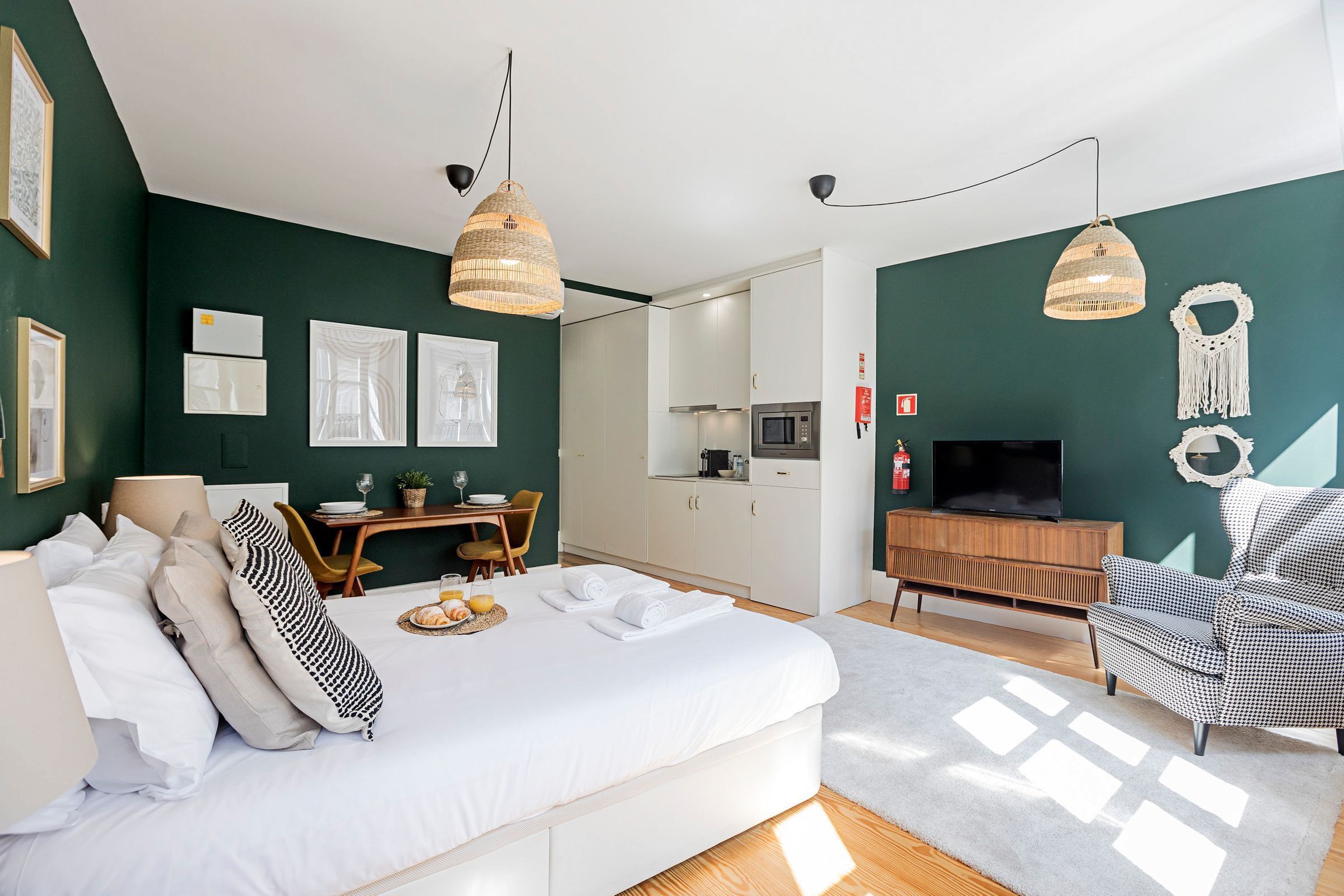 Quarto de hotel moderno com uma cama grande, área de refeições, televisão e cozinha compacta.
