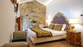 Quarto com parede de pedra, cabeceira estofada, cama com almofadas estampadas, mesa de cabeceira com abajur e uma cadeira.