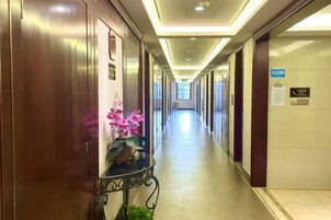 Corredor de hotel com portas, balcão de recepção e placa indicando a área dos elevadores.