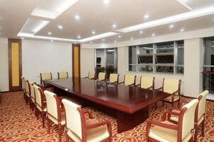 Uma sala de conferências com uma grande mesa retangular rodeada por cadeiras, um tapete estampado e uma janela com persianas.