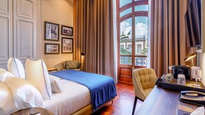 Quarto de hotel com uma cama, uma escrivaninha com telefone, uma cadeira e vista para um edifício pela janela.