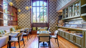 Restaurante com piso de madeira, uma mesa de jantar central rodeada de cadeiras e uma grande janela com vista para palmeiras.