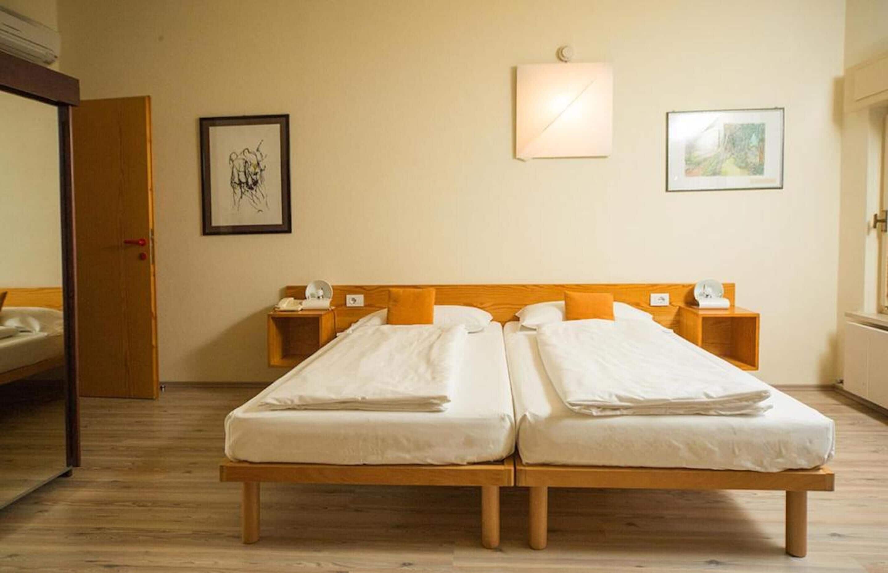 Uma cama de casal com roupa de cama branca, duas mesas de cabeceira com abajures e obras de arte nas paredes.