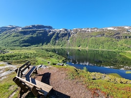 Um banco de madeira com vista para um lago tranquilo e montanhas ao fundo.