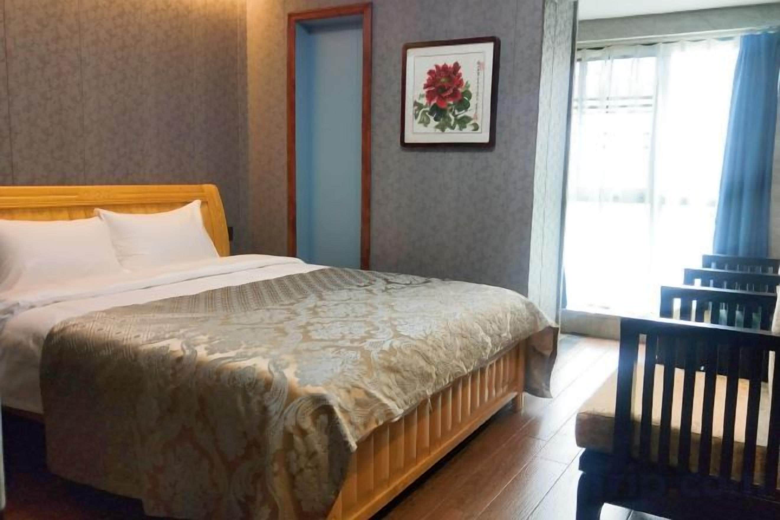 Quarto de hotel com cama, uma cadeira, um quadro na parede e janela com cortinas.