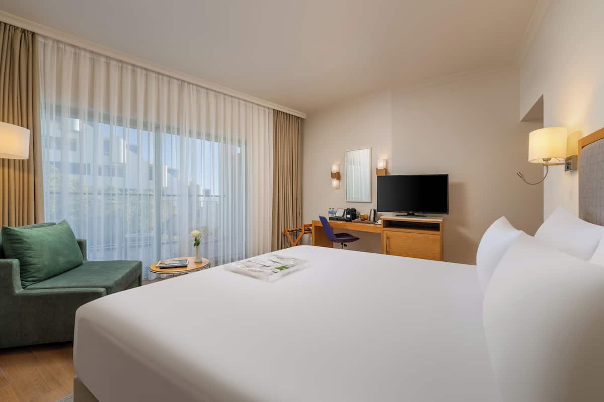 Quarto de hotel com uma cama grande, uma escrivaninha, uma televisão e um sofá.