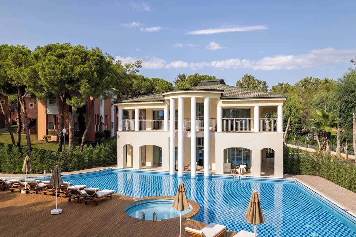 Um edifício de dois andares com área de piscina, incluindo cadeiras de descanso e guarda-sóis.