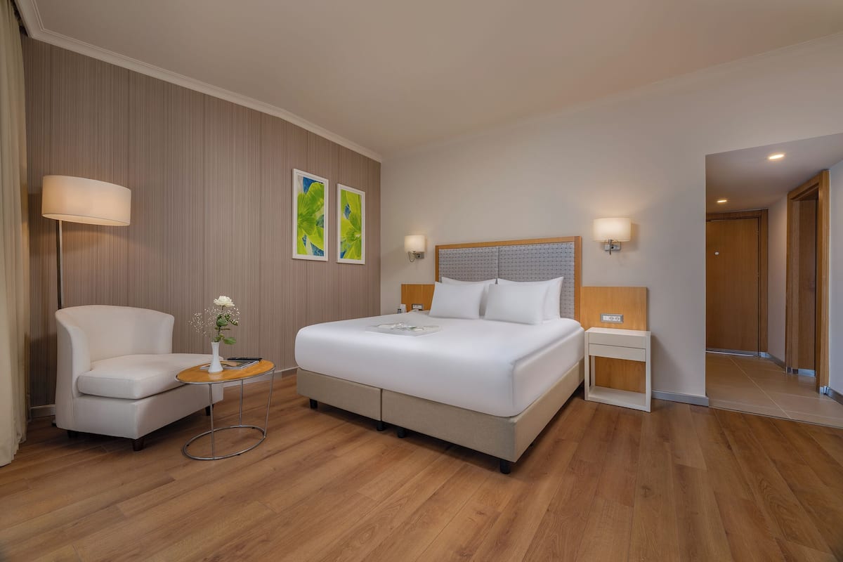 Quarto de hotel com cama, cadeira, mesa pequena e mesa de cabeceira.