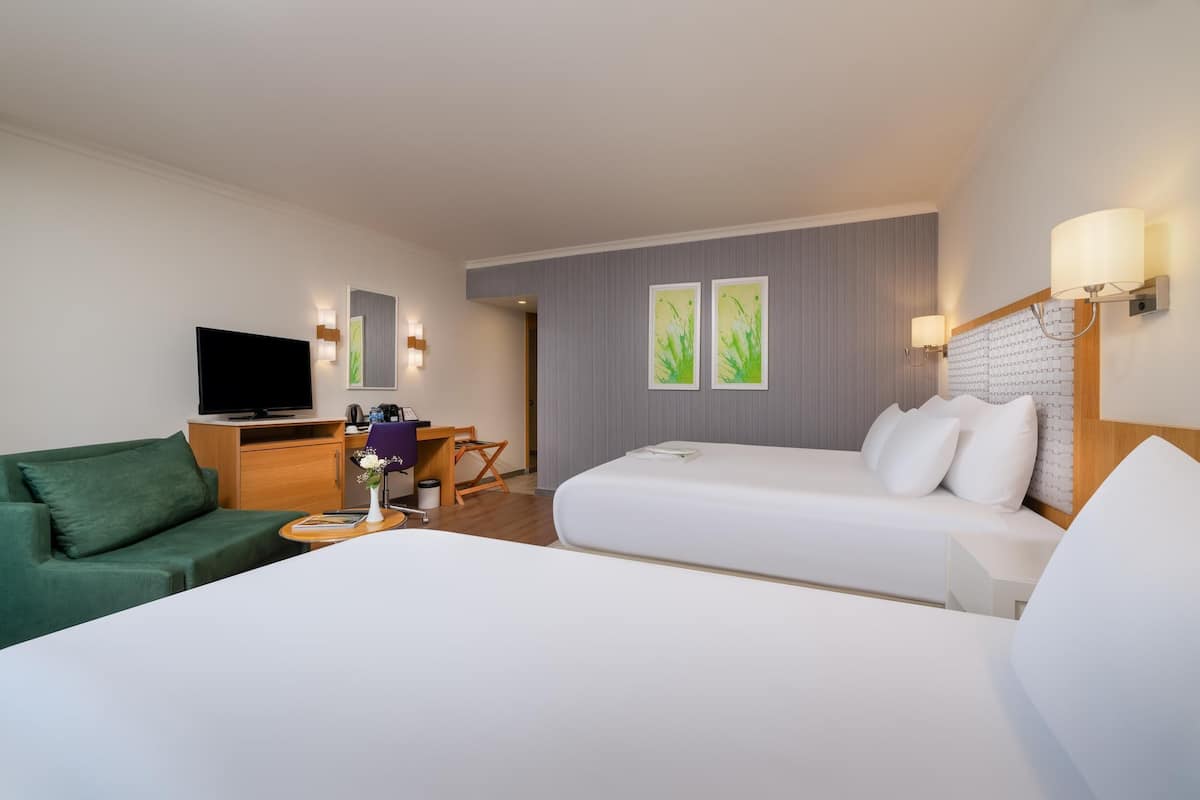 Quarto de hotel com uma cama, um sofá verde, uma escrivaninha com um computador e uma televisão.
