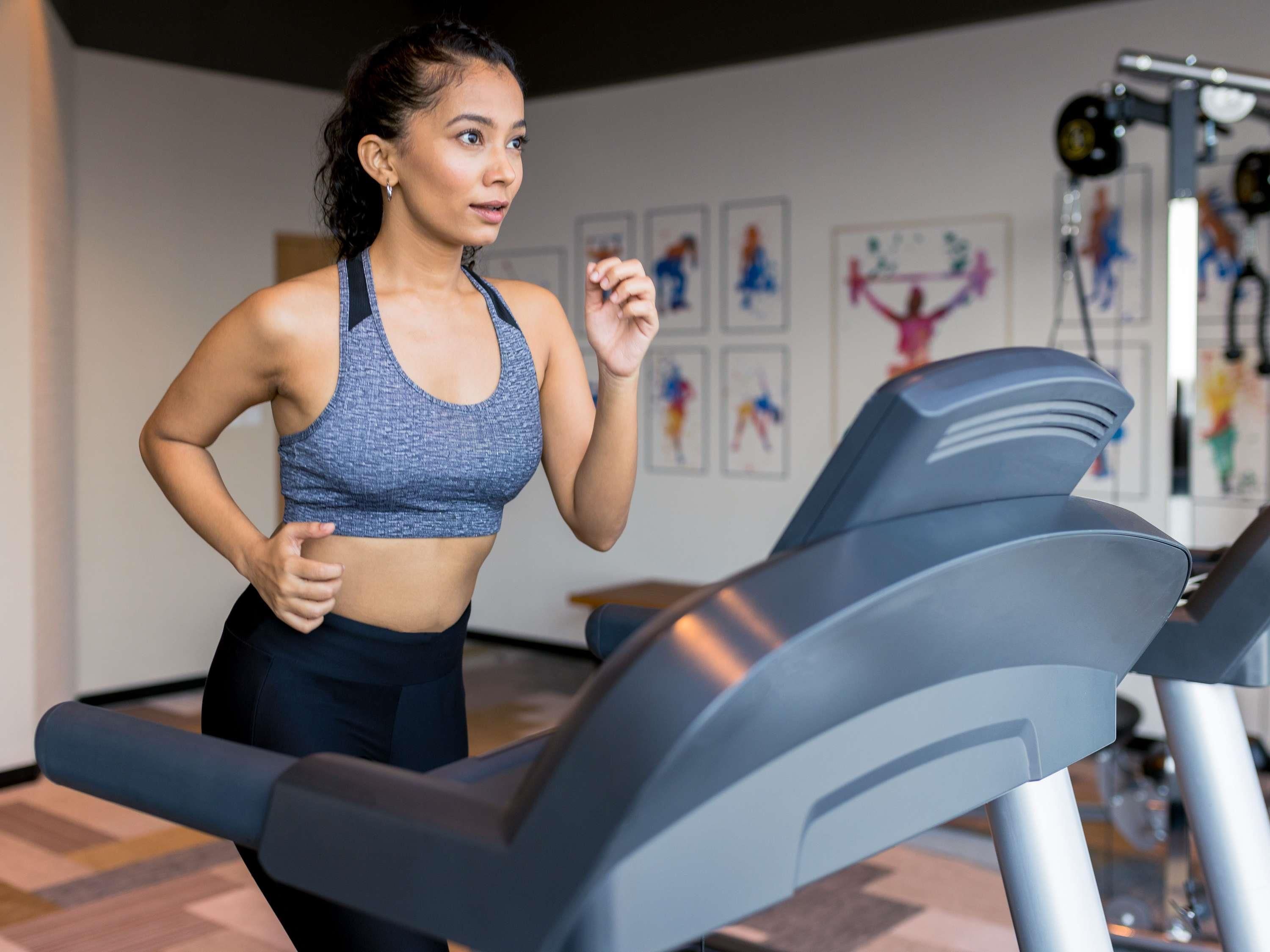 Uma pessoa corre na esteira numa academia, com equipamentos de exercício e obras de arte nas paredes.
