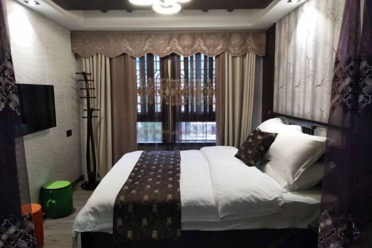 Quarto de hotel com cama, cortinas, televisão e um cesto de lixo verde.