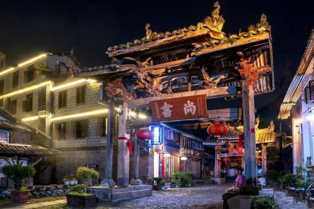 Um edifício tradicional com portão de madeira, degraus de pedra e uma placa com caracteres chineses.