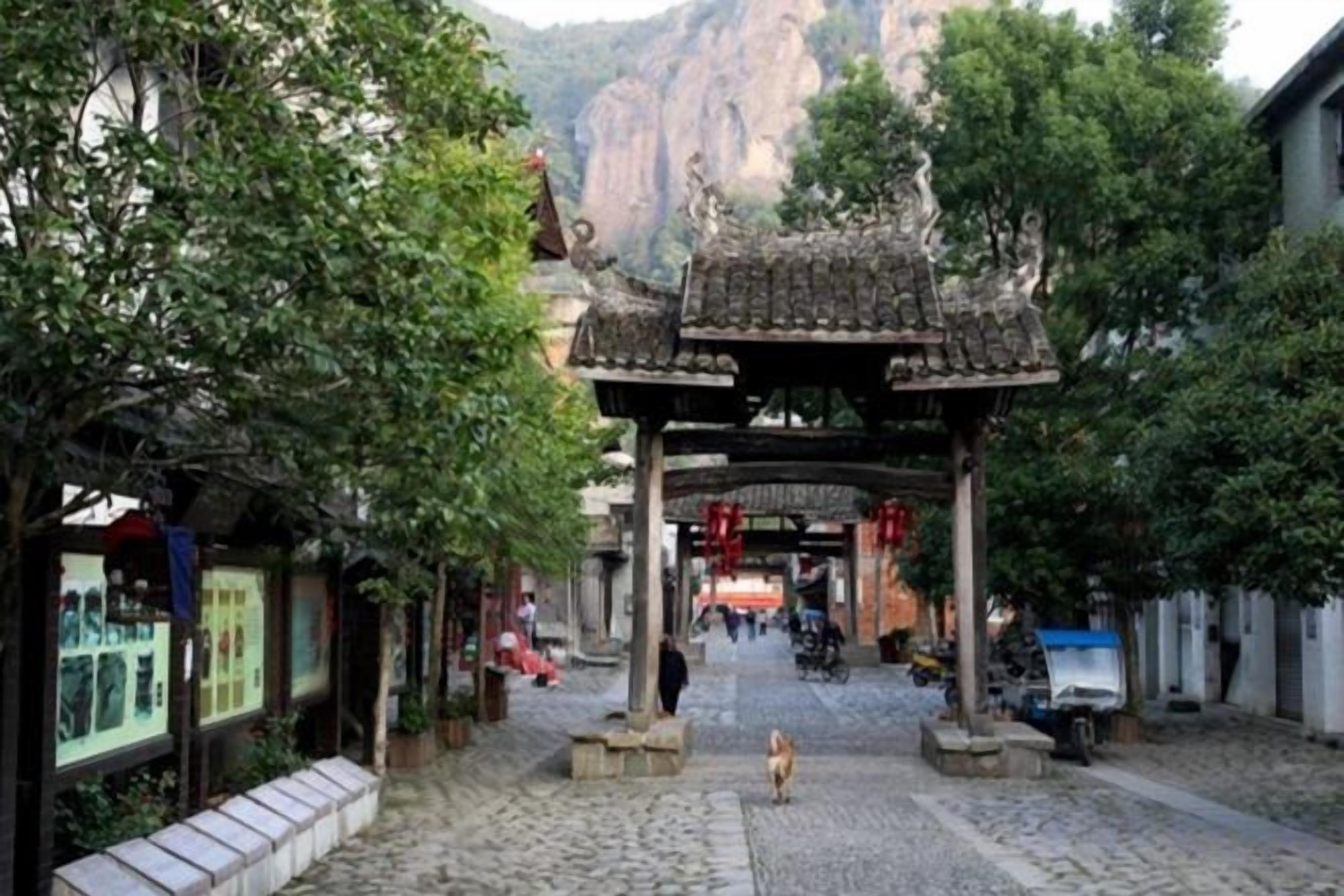Um portão tradicional chinês com telhado de azulejos, dando acesso a uma rua de paralelepípedos.
