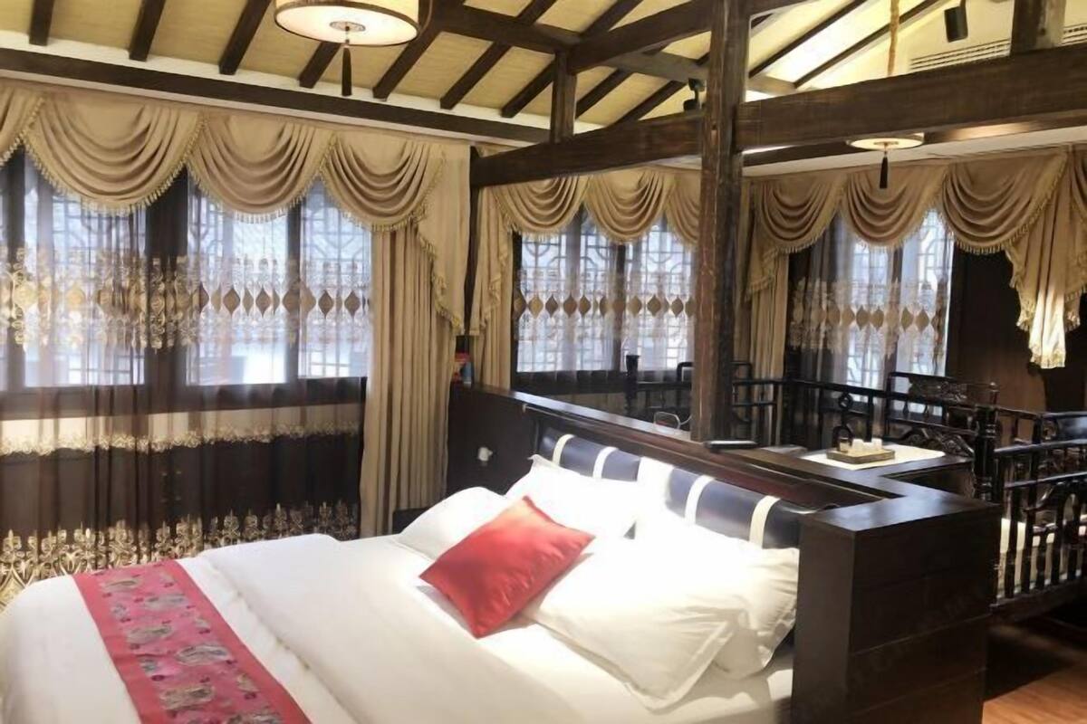 Quarto com cama grande, cabeceira de madeira escura e janela com cortinas leves.