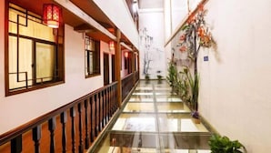 Um corredor com piso de vidro, guarda-corpo de madeira e decoração tradicional, incluindo lanternas e plantas.