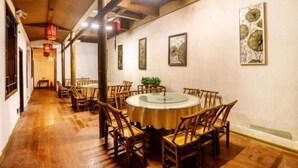 Uma área de refeições com mesas e cadeiras de madeira, uma mesa redonda de vidro e obras de arte penduradas na parede.