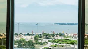 Vista pela janela de uma área arborizada, com caminhos, árvores e um corpo d'água ao longe.