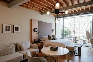 Quarto moderno com teto de madeira, uma cama, um sofá, uma mesa de jantar e uma janela grande com vista para o verde.