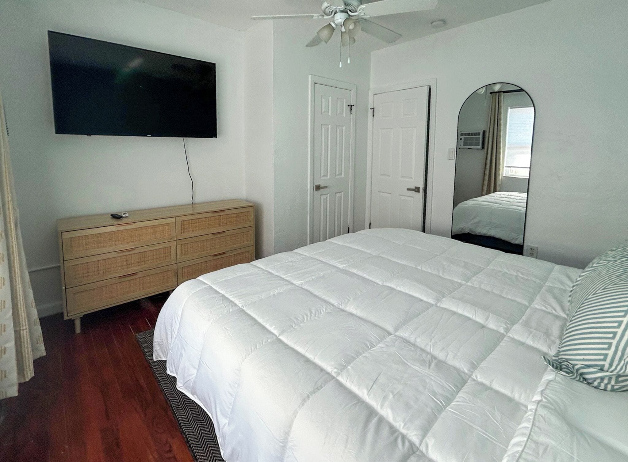 Quarto com cama, penteadeira, televisão na parede e ventilador de teto.