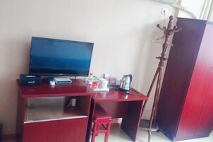Quarto com televisão, escrivaninha com computador, chaleira e armário.