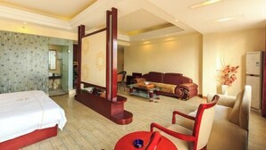 Quarto de hotel com uma cama, uma poltrona vermelha, um sofá, uma mesinha e um biombo decorativo.