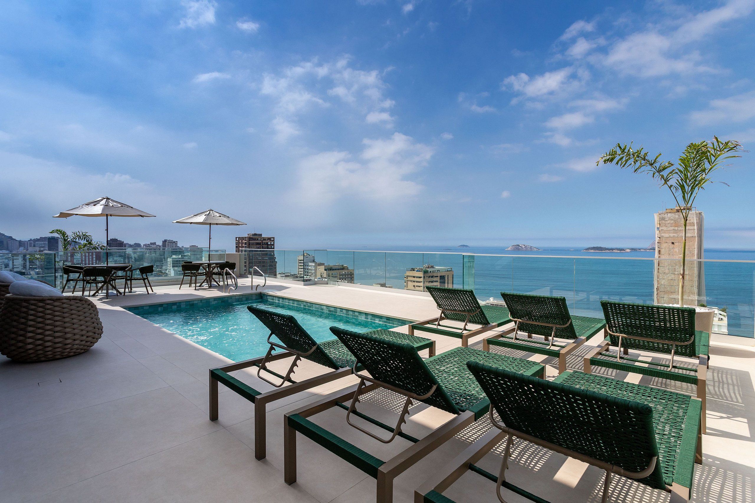 Área de piscina no terraço com espreguiçadeiras e guarda-sóis, com vista para a paisagem urbana e o mar.