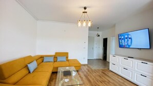 Uma sala de estar com um sofá amarelo, uma mesa de centro de vidro e um armário branco.