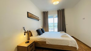 Quarto com cama de madeira, mesa de cabeceira com abajur, janela com cortinas e vista para o exterior.
