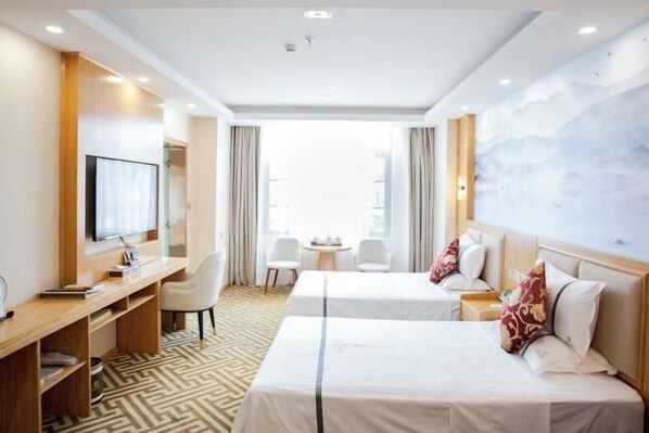 Quarto de hotel com duas camas, uma escrivaninha, televisão e vista para a cidade.