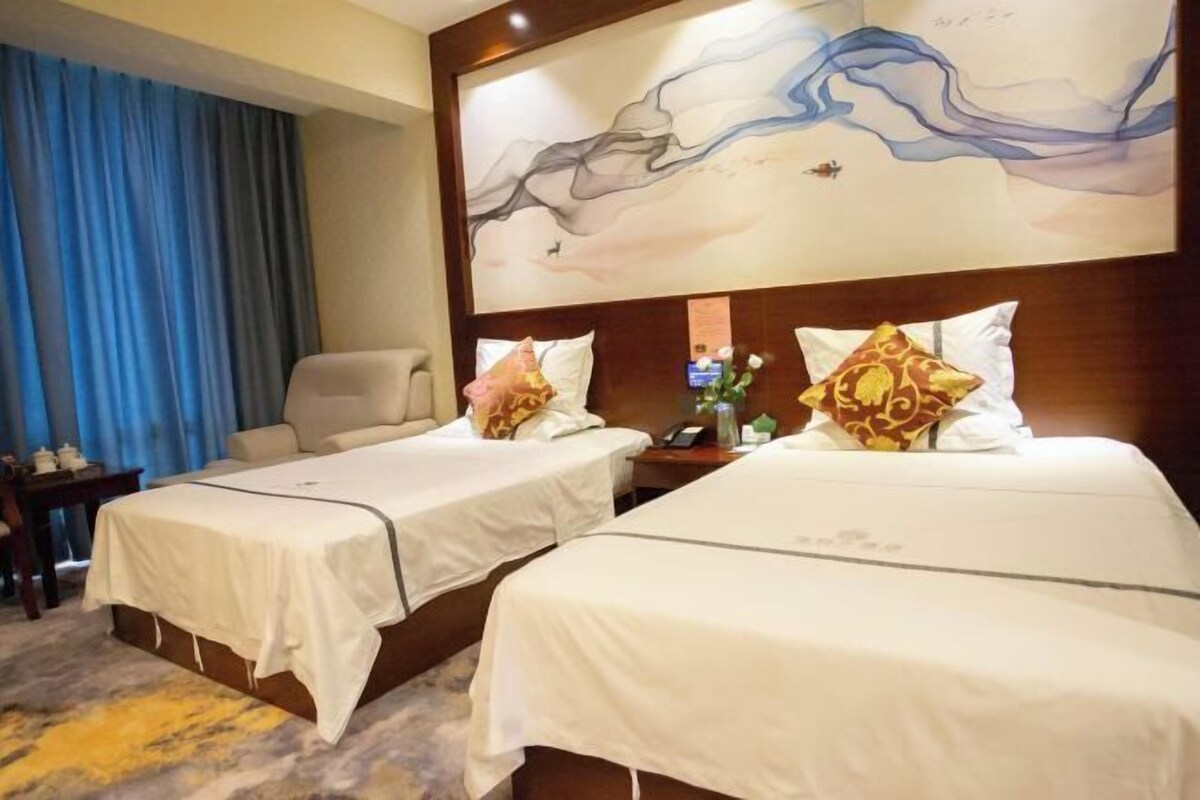 Quarto de hotel com duas camas, um quadro abstrato grande na parede, uma mesa com telefone e uma cadeira.