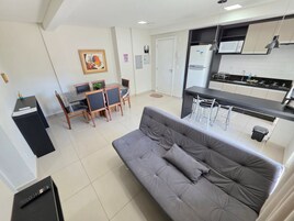 Um apartamento moderno com sofá cinzento, área de jantar com mesa e cadeiras, cozinha com micro-ondas e um quadro na parede.