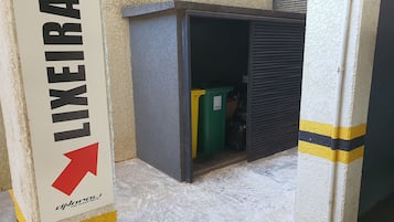 Uma porta com uma placa indicando direção, um depósito pequeno e uma lixeira.