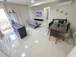 Uma sala de estar moderna com área de jantar, um sofá, uma cafeteira e uma TV de tela plana na parede.